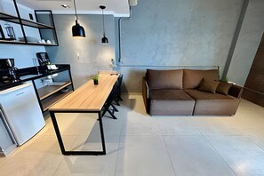 Cozinha moderna com mesa de madeira, cadeiras com estrutura preta, sofá marrom e iluminação pendente.