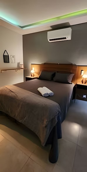 Quarto moderno com cama grande, mesas de cabeceira, ar-condicionado na parede e luminária no teto.