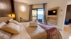 Quarto de hotel com cama grande, televisão, varanda e vista, e escrivaninha com cadeira.