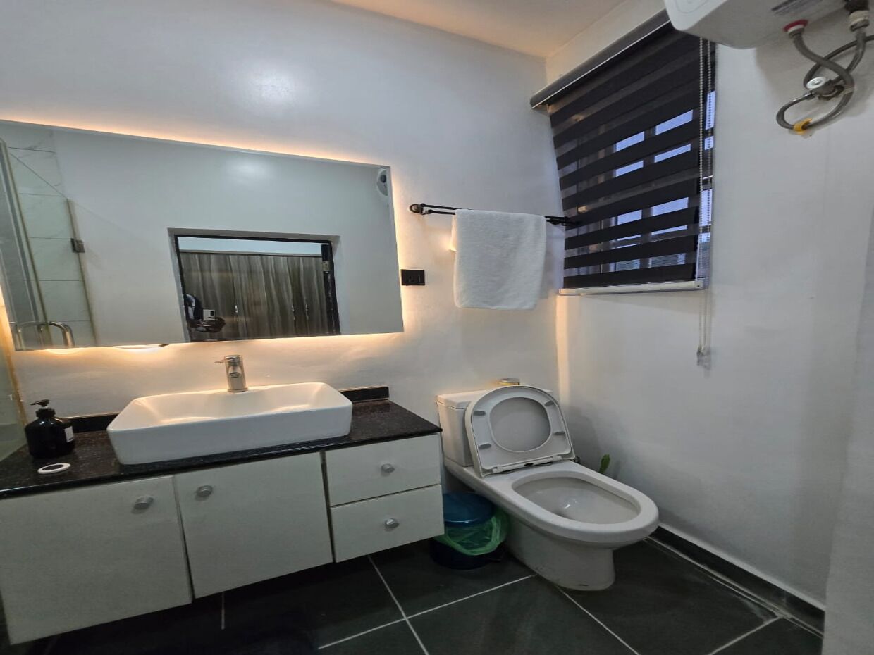Uma casa de banho com lavatório branco, espelho e sanita.
