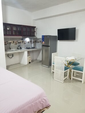 Quarto de hotel compacto com cozinha compacta, cama, televisão e pequena área de refeições.