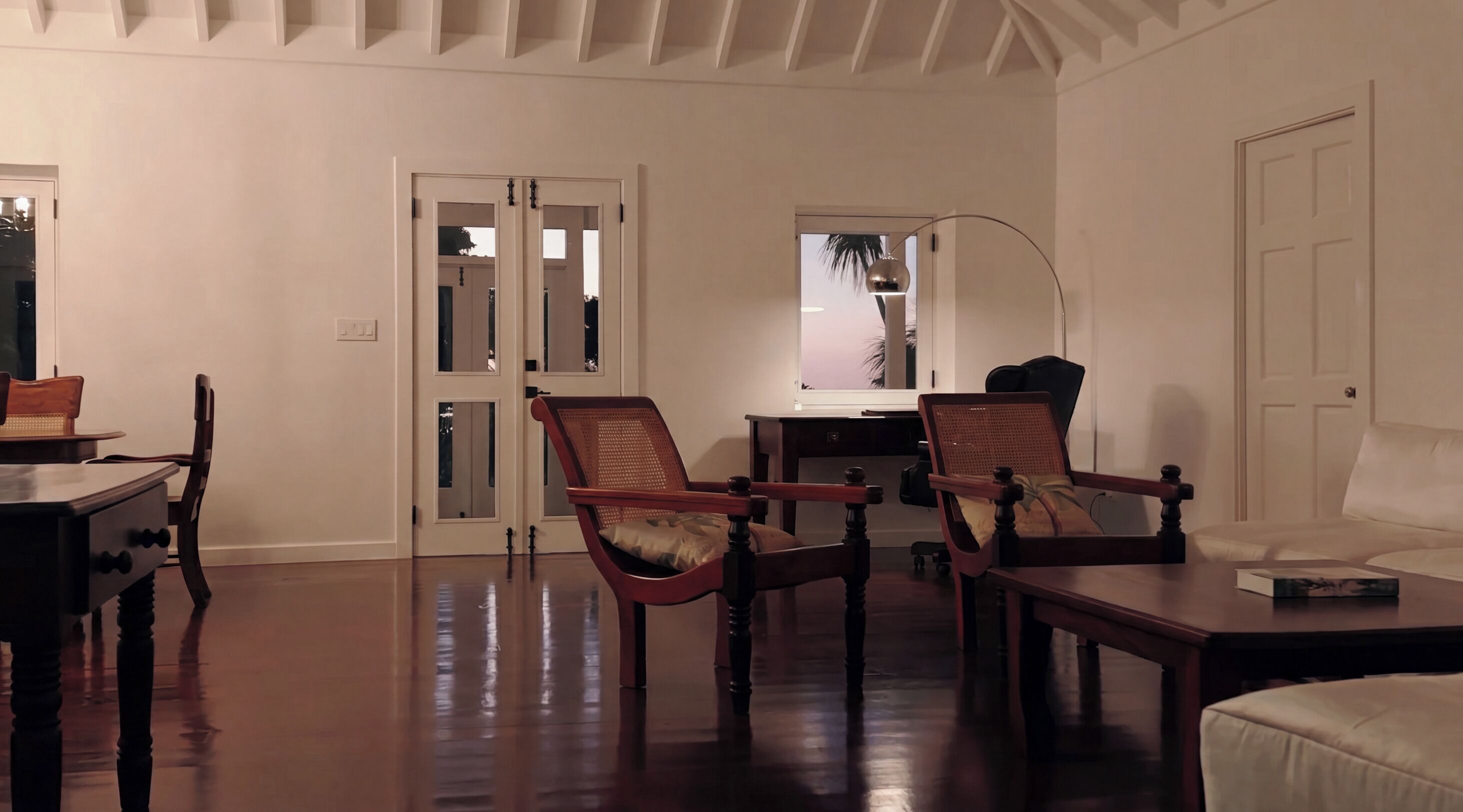 Um quarto espaçoso com piso de madeira, uma escrivaninha com cadeira, dois poltronas, um sofá e uma porta com painéis de vidro.