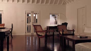 Um quarto espaçoso com piso de madeira, uma escrivaninha com cadeira, dois poltronas, um sofá e uma porta com painéis de vidro.