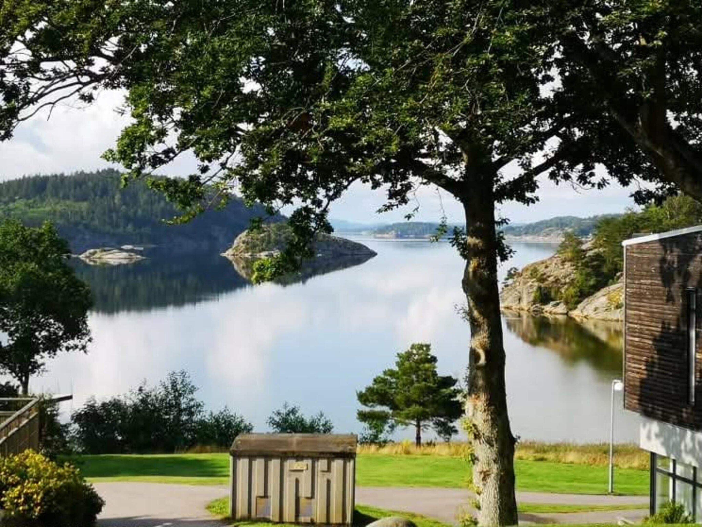 Vista para o lago, com uma cabana de madeira e céu claro.