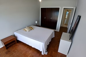 Quarto com cama, mesa de cabeceira, guarda-roupa e espelho.