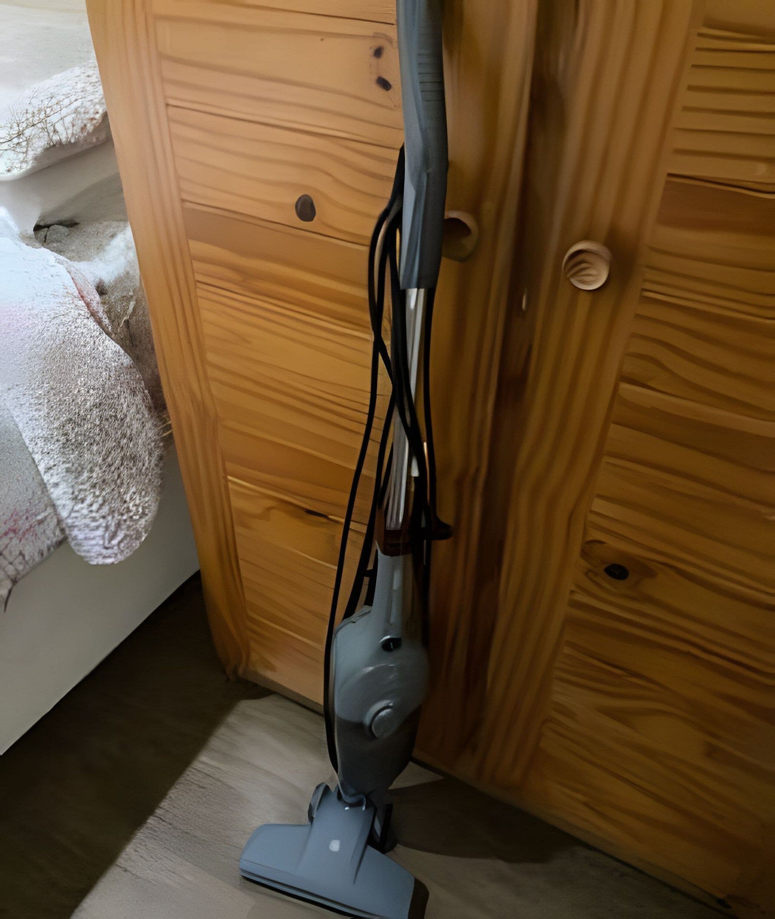 Aspirador de pó num quarto com armários de madeira e chão de azulejos.