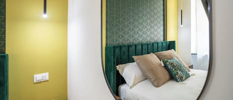 Uma cama com cabeceira verde e várias almofadas, uma mesa de cabeceira com abajur e uma tomada na parede.