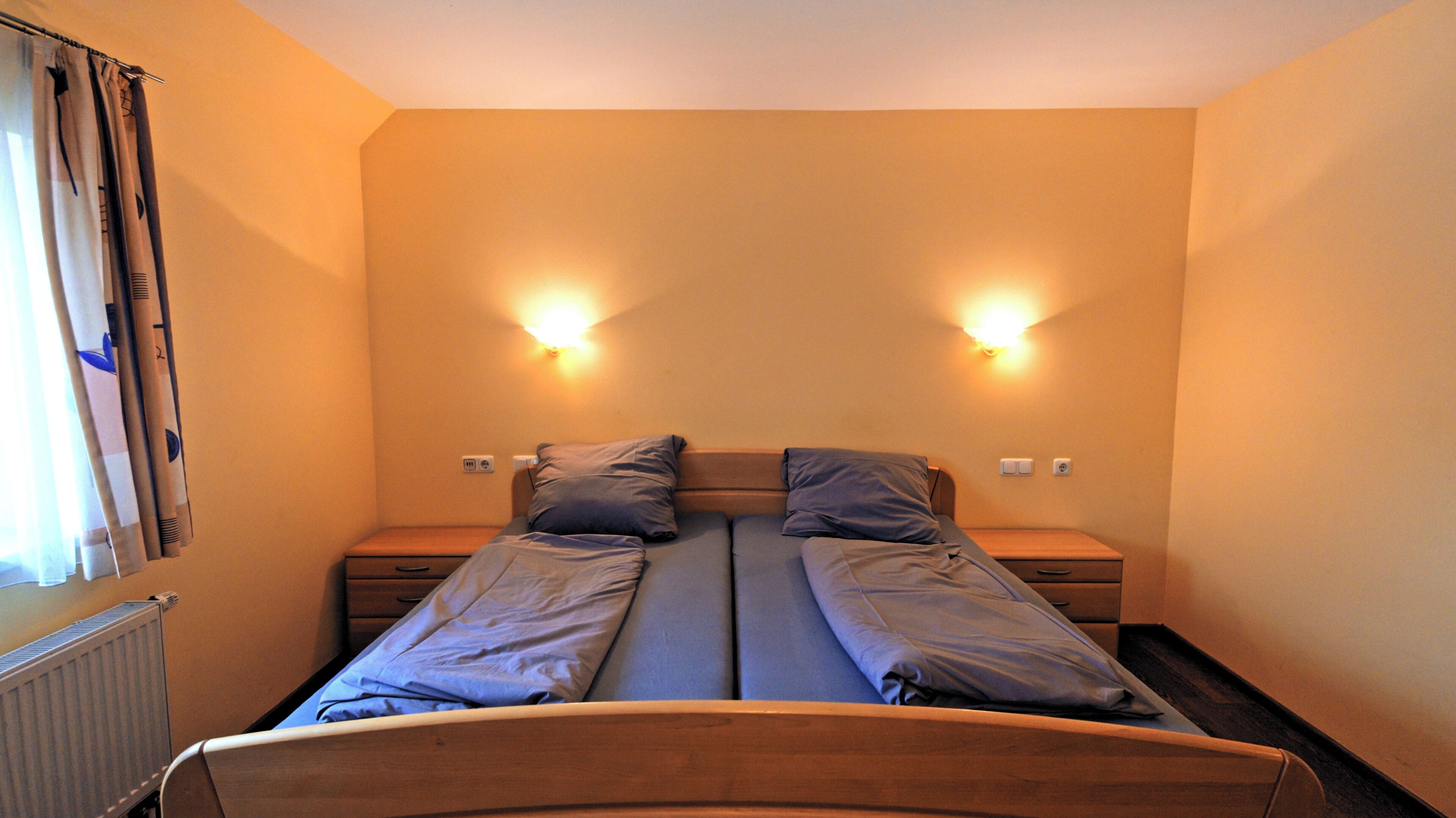 Quarto duplo com duas camas de solteiro, mesas de cabeceira e luminárias fixadas na parede.