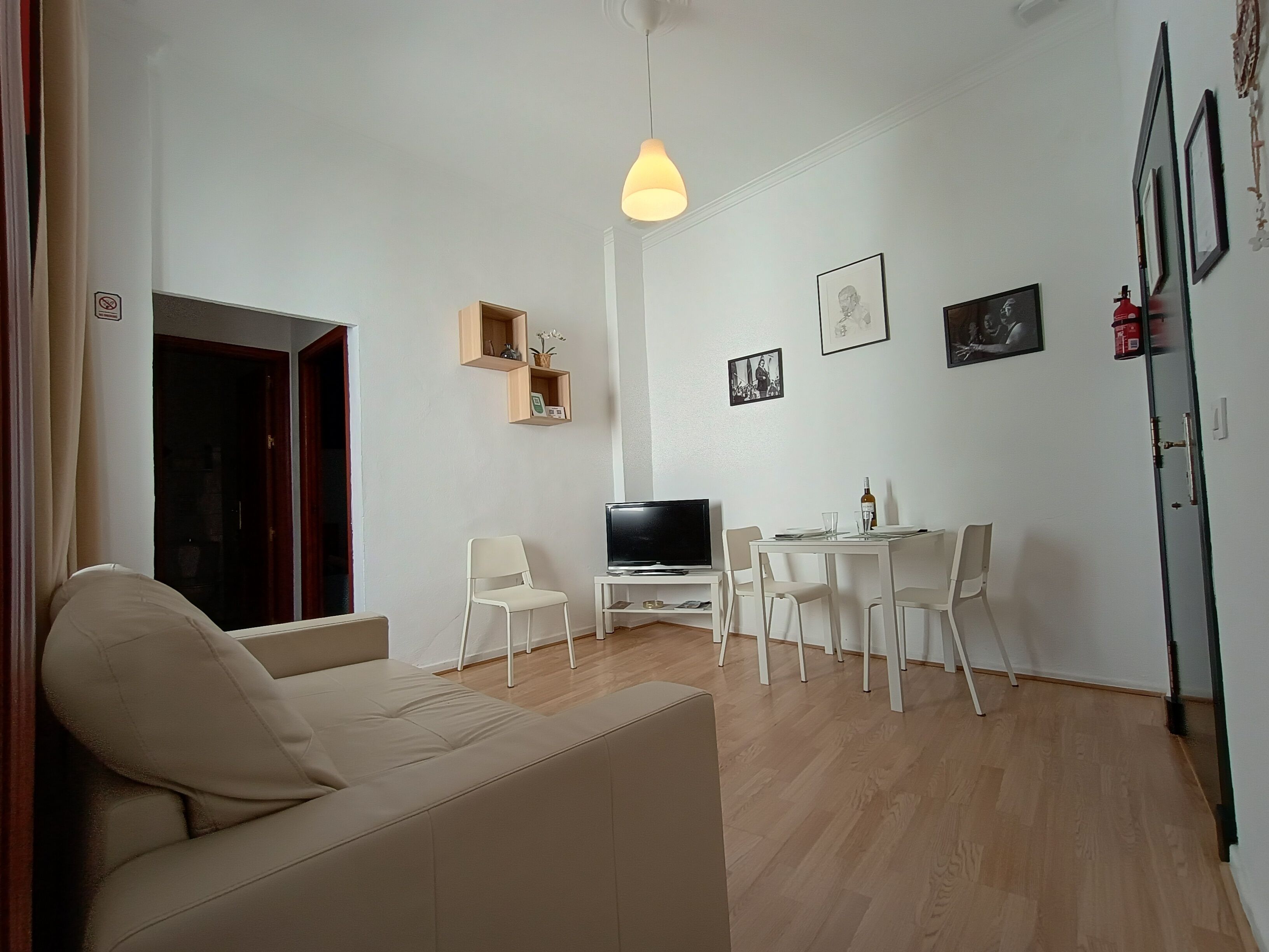 Sala de estar com sofá, televisão, mesa de jantar, cadeiras e luminária pendente.
