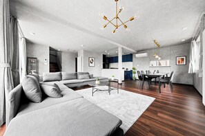 Uma sala de estar moderna com um sofá seccional, uma área de jantar e uma cozinha ao fundo.