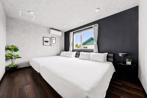 Quarto moderno com uma cama grande, uma planta em vaso e vista para uma casa pela janela.