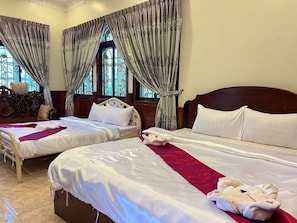 Quarto de hotel com duas camas, uma cabeceira de madeira, um tapete vermelho e uma janela com cortinas.