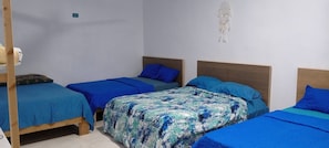 Quarto com três camas, cada uma com roupa de cama azul e cabeceira de madeira.