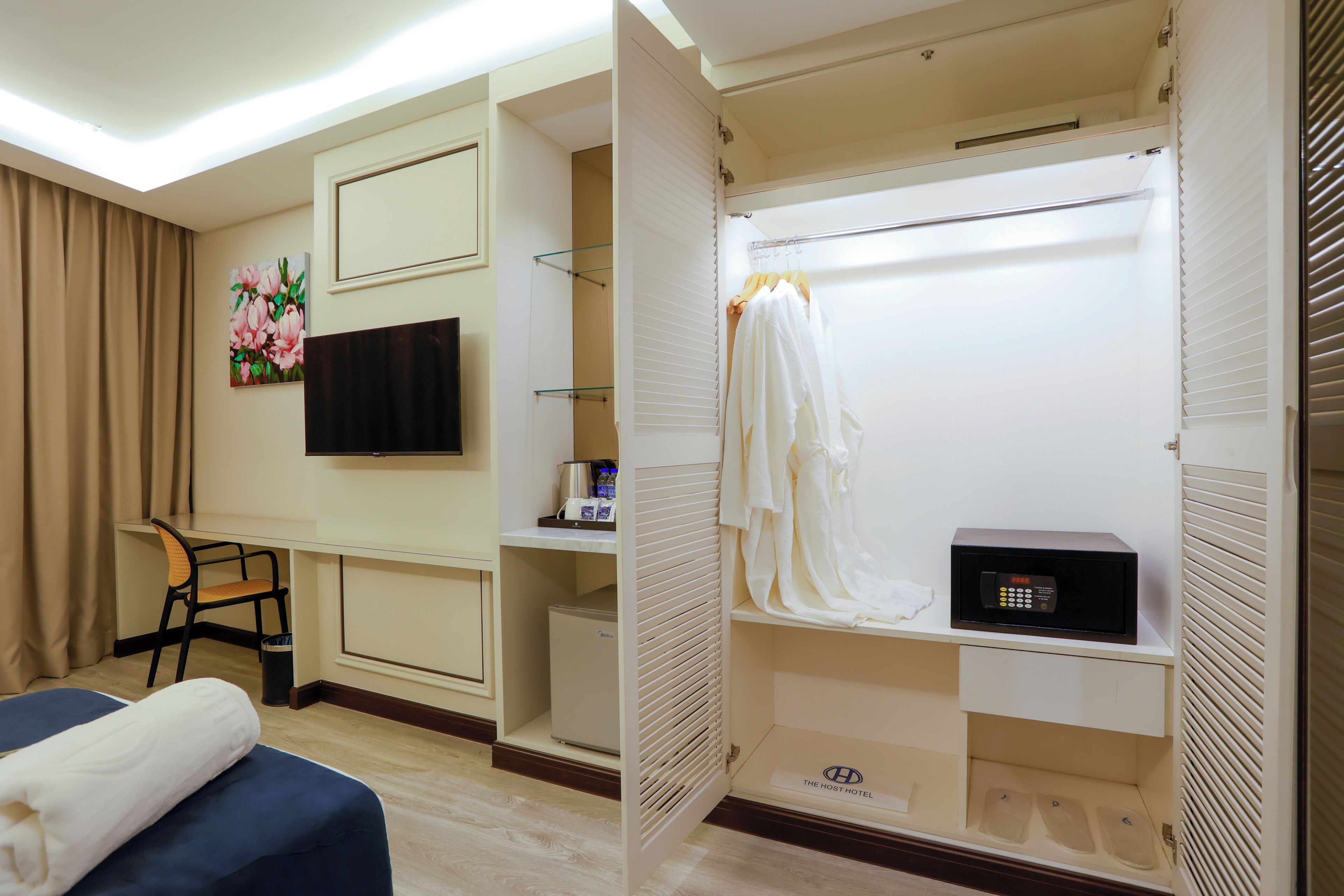 Quarto de hotel com cama, escrivaninha, televisão, minibar e closet espaçoso com roupão.