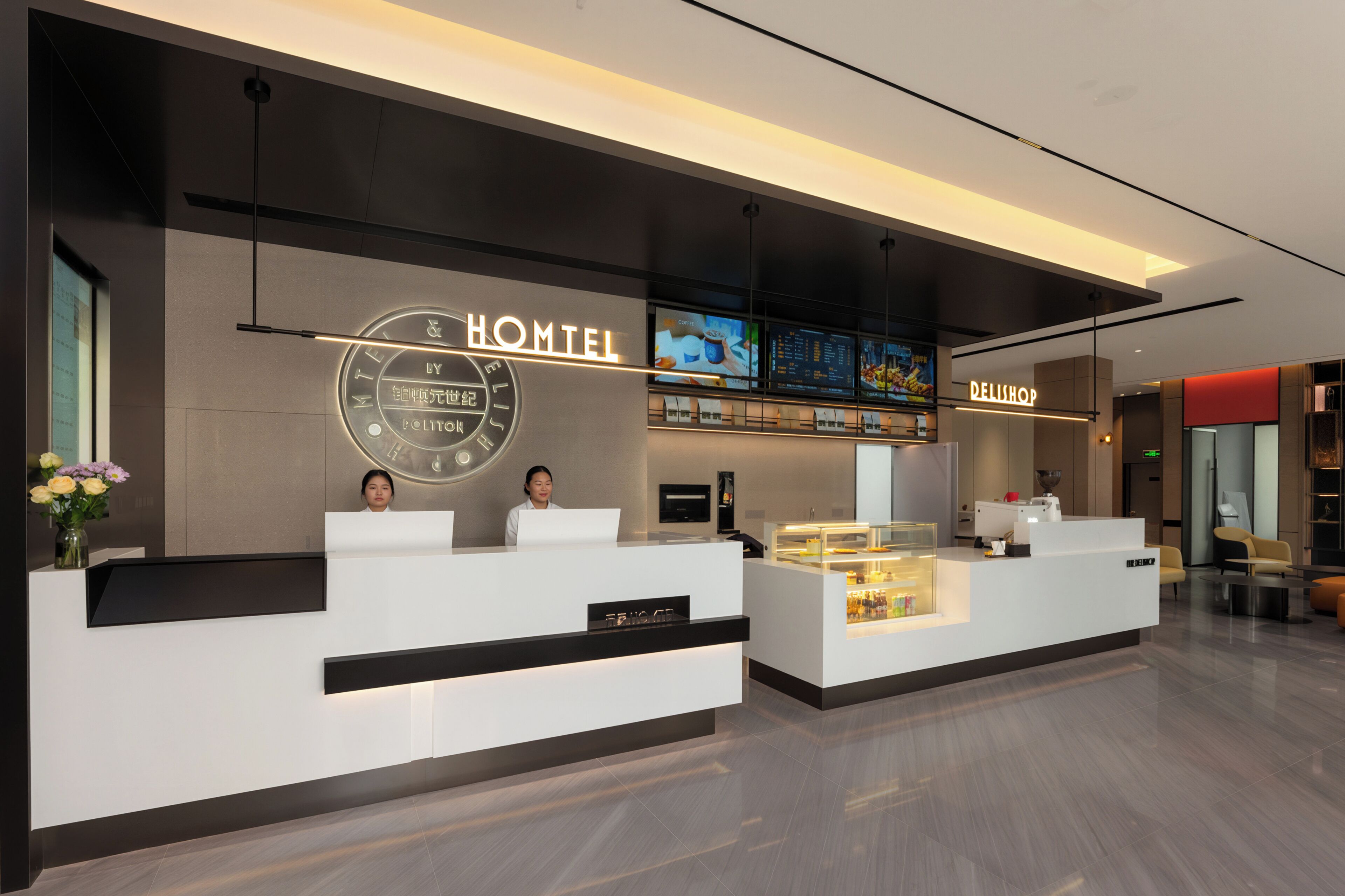 Uma receção de hotel moderna com um ecrã digital, um café e uma área de estar.