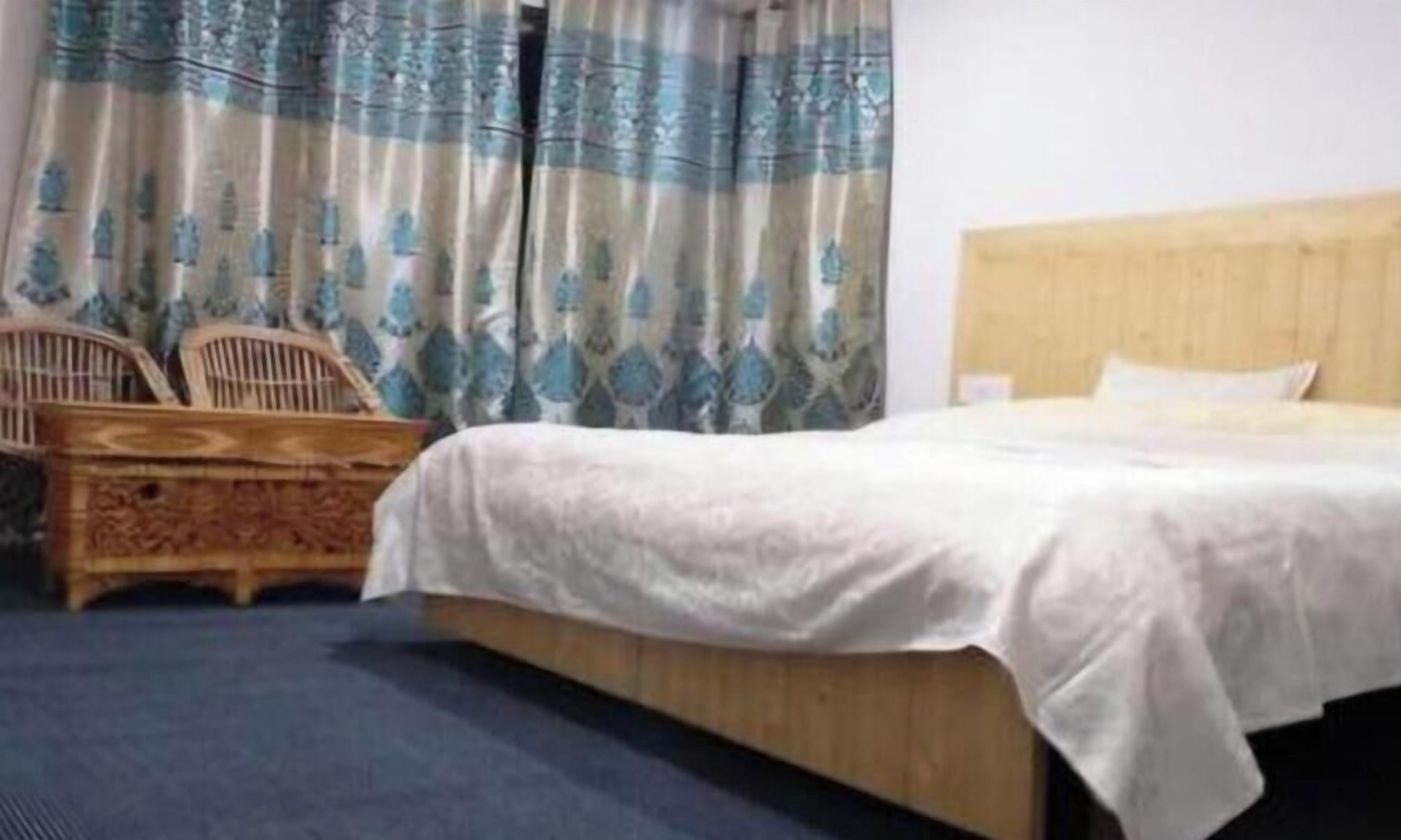 Quarto com cama, cabeceira de madeira, duas cadeiras e cortina com padrão de árvore.