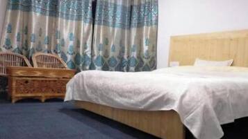 Quarto com cama, cabeceira de madeira, duas cadeiras e cortina com padrão de árvore.