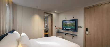 Quarto de hotel com uma cama, televisão fixada na parede e porta de madeira.
