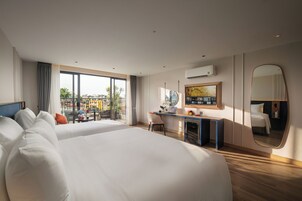 Quarto de hotel com duas camas grandes, uma secretária com um laptop, um espaço de refeições com mesa e cadeiras, e uma janela ampla com vista para a cidade.