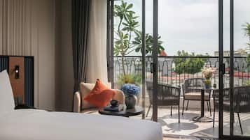 Quarto de hotel com cama, sofá, mesa com um vaso de flores e varanda com vista para a cidade.