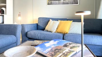 Uma sala de estar com um sofá azul, uma mesa de centro com um livro e um abajur.