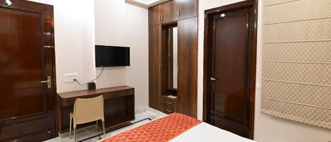 Quarto de hotel com cama, escrivaninha, cadeira, televisão e guarda-roupa.