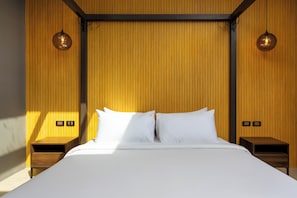 Quarto com cabeceira de madeira, uma cama grande com roupa de cama branca, duas mesas de cabeceira e duas luzes pendentes.