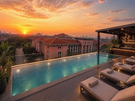 Piscina no terraço com espreguiçadeiras e bar, com vista para o horizonte urbano ao pôr do sol.