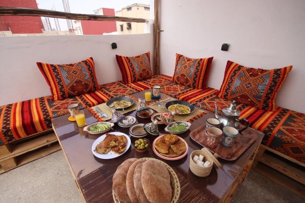 Uma área de refeições com uma mesa posta para refeição, cercada por almofadas coloridas e estampadas.