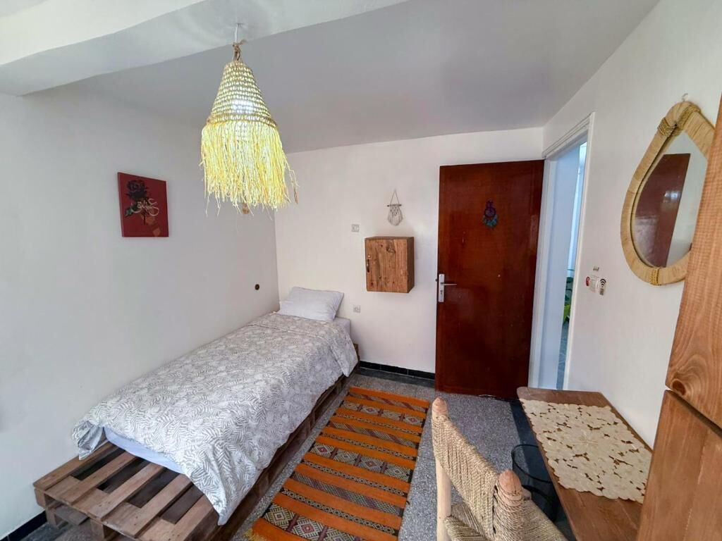 A bedroom with a bed, a hanging light fixture, a wooden door, and a small rug.