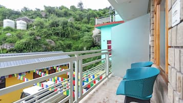 Uma varanda com vista para uma encosta verdejante e coberta de vegetação, uma mesa pequena com orações coloridas tremulando e duas cadeiras azuis.