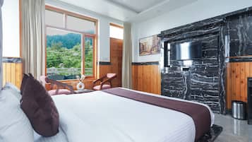 Quarto com cama, TV fixada em parede de pedra, janela com vista para vegetação e porta de madeira.
