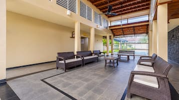 Amplo espaço interno com móveis de vime, ventilador de teto e grandes janelas que proporcionam luz natural.