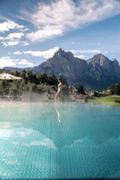 Piscina límpida com montanhas ao fundo, rodeada por vegetação e edifícios.