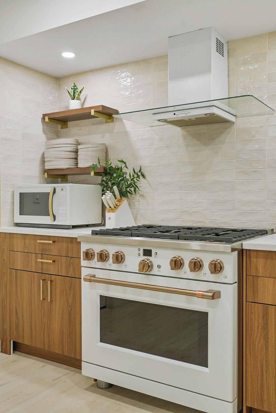 Uma cozinha com fogão, forno, micro-ondas e prateleiras com louças e plantas.