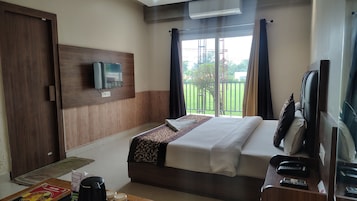 Quarto de hotel com cama, televisão na parede, janela com cortinas e vista para a varanda.