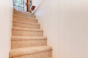 Uma escadaria carpetada com corrimão, que leva a um patamar com uma janela e uma porta.