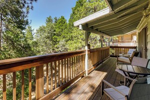 Um deck de madeira com móveis de exterior, cercado por árvores.