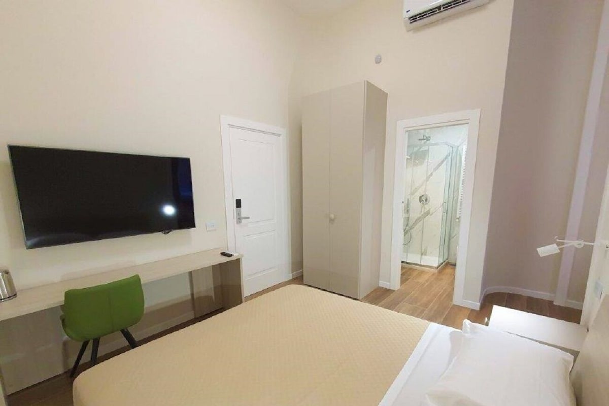 Quarto de hotel com cama, televisão na parede, secretária com cadeira e guarda-roupa.