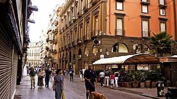Uma rua com pedestres, um café e um edifício com uma placa.