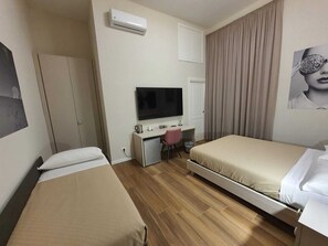 Quarto de hotel com duas camas, uma escrivaninha com televisão, ar condicionado e uma janela com cortinas.