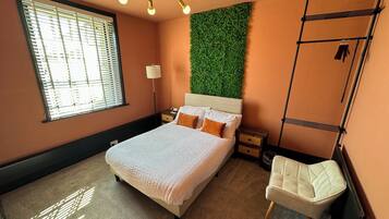 Quarto com cama, mesa de cabeceira, abajur, parede verde, janela com persianas e guarda-roupa.