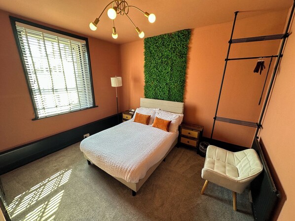 Quarto com cama, mesa de cabeceira, abajur, parede verde, janela com persianas e guarda-roupa.