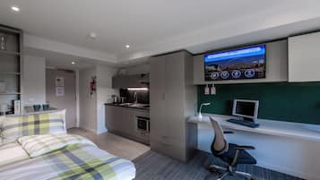 Quarto de hotel moderno com uma cama, uma escrivaninha, um computador e uma televisão.