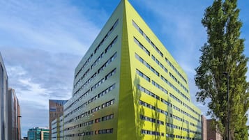 Um edifício moderno com formato triangular distinto, várias janelas e uma entrada imponente.