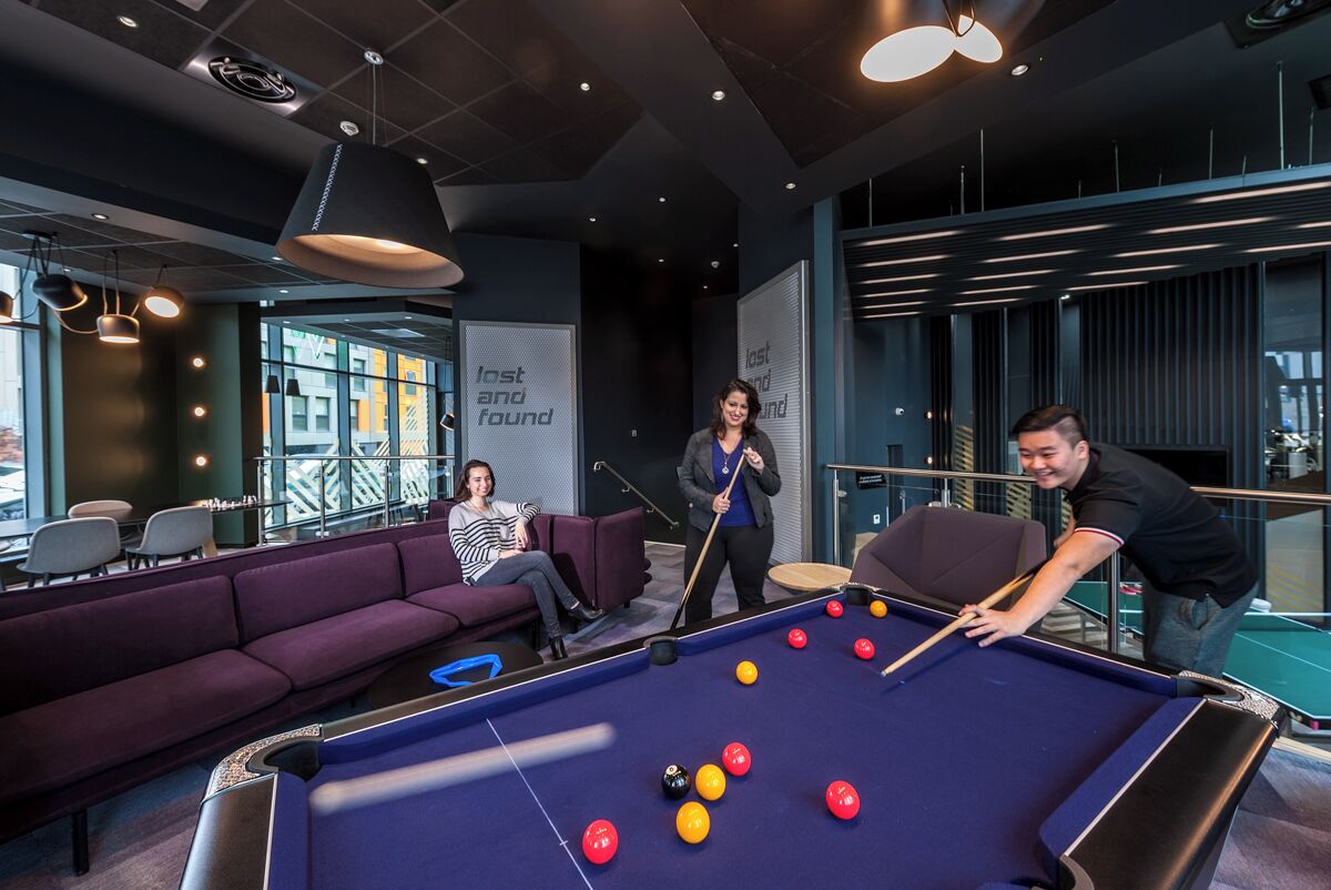 Uma mesa de bilhar em uma área de lounge moderna, com um sofá e uma janela grande.