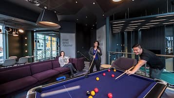 Uma mesa de bilhar em uma área de lounge moderna, com um sofá e uma janela grande.