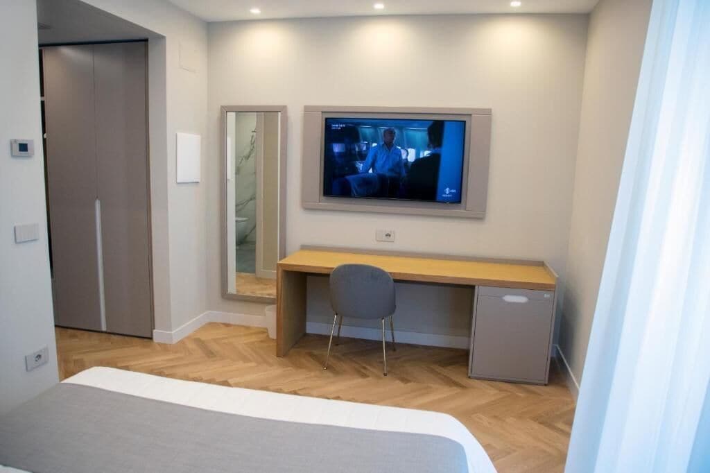Quarto com cama, escrivaninha, cadeira, televisão e guarda-roupa.