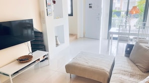 Uma sala de estar moderna com televisão de tela plana, um sofá, uma mesa de centro e uma área de jantar com mesa e cadeiras.