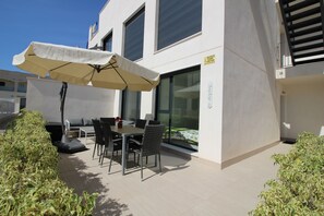 Um pátio ao ar livre com mesa, cadeiras, um guarda-sol grande e um sofá.